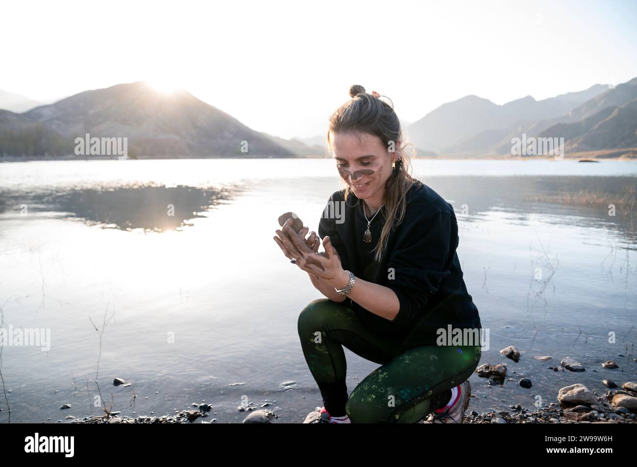 Woman putting mud on hands and face while enjoying outdoors in nature ...
