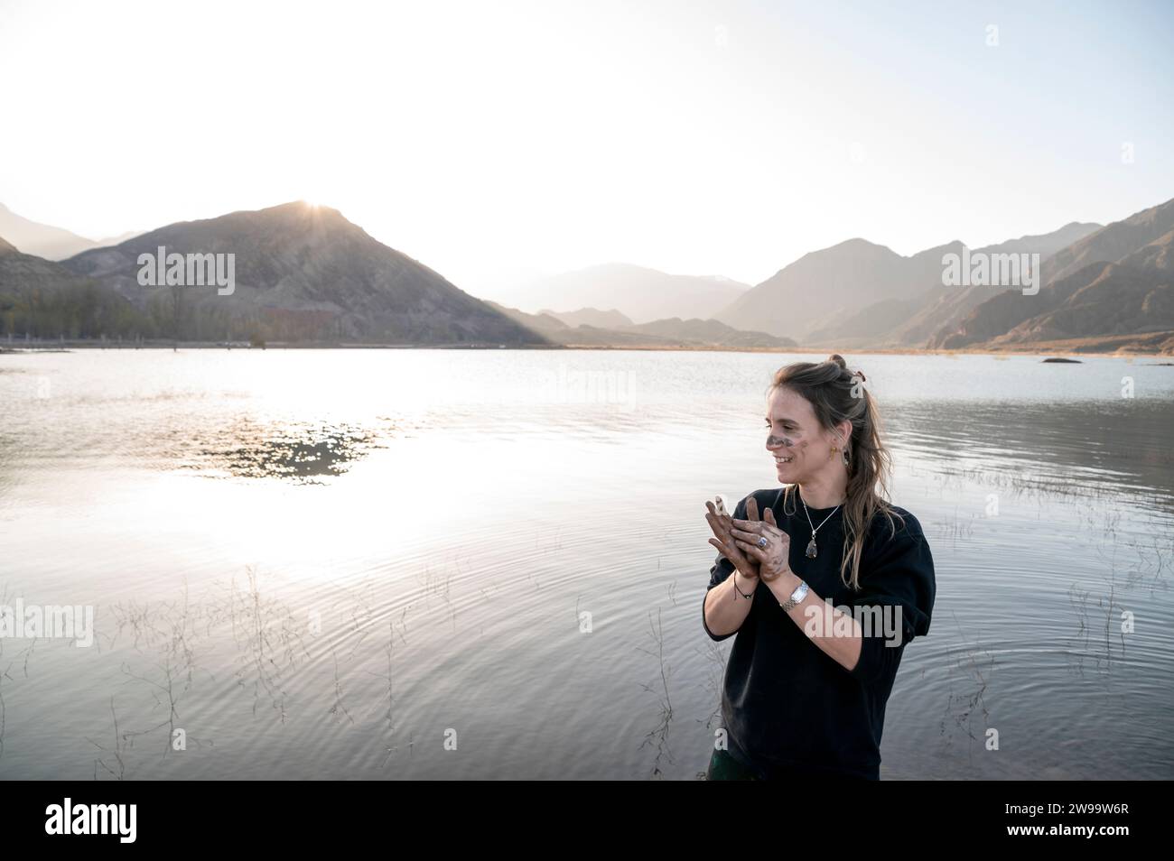 Woman putting mud on hands and face while enjoying outdoors in nature ...