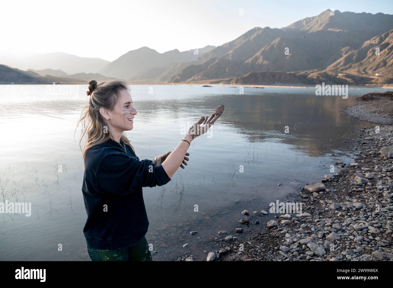 Woman putting mud on hands and face while enjoying outdoors in nature ...