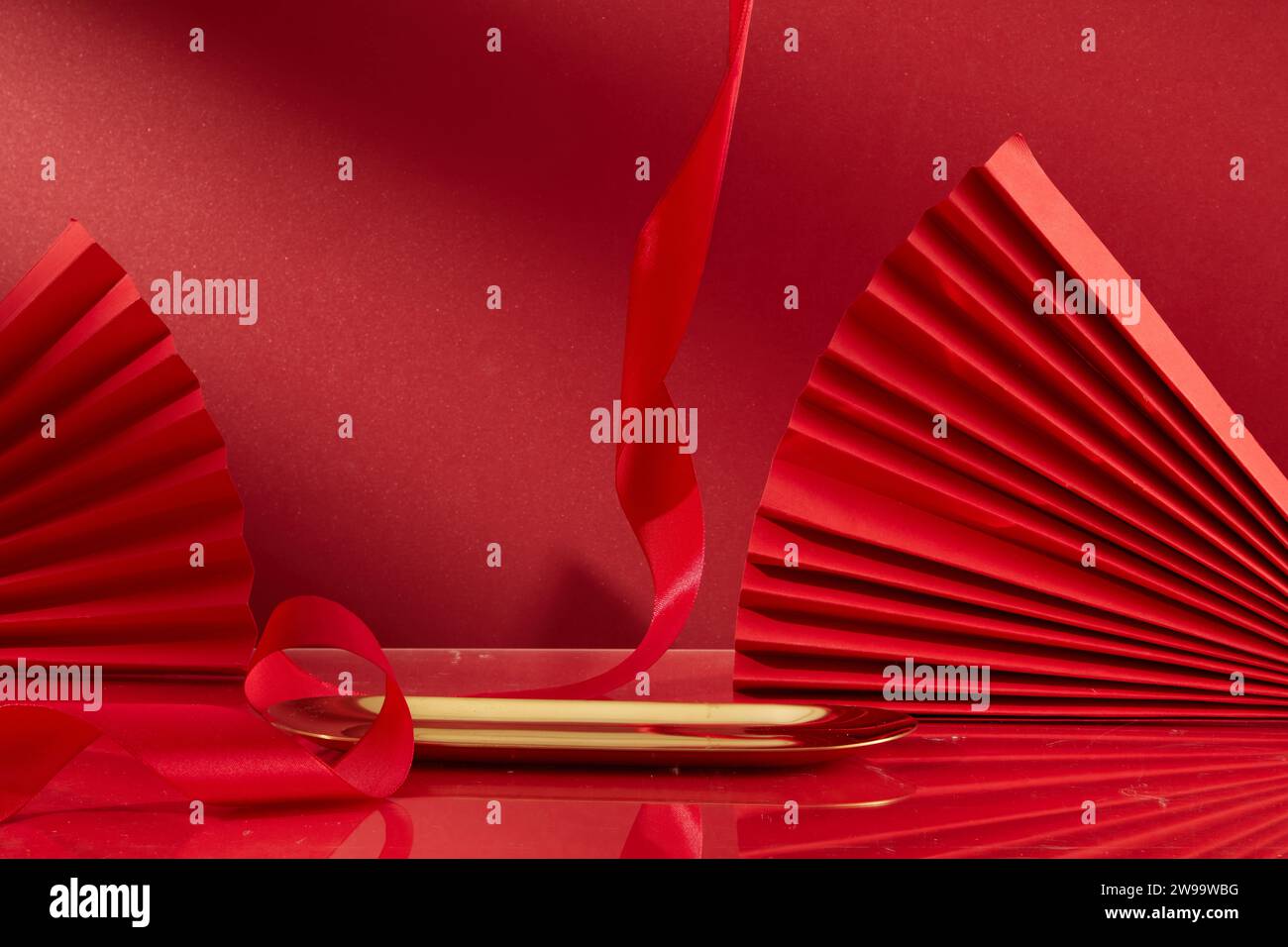 Two paper fans, a ribbon and a metal tray are displayed on a red ...