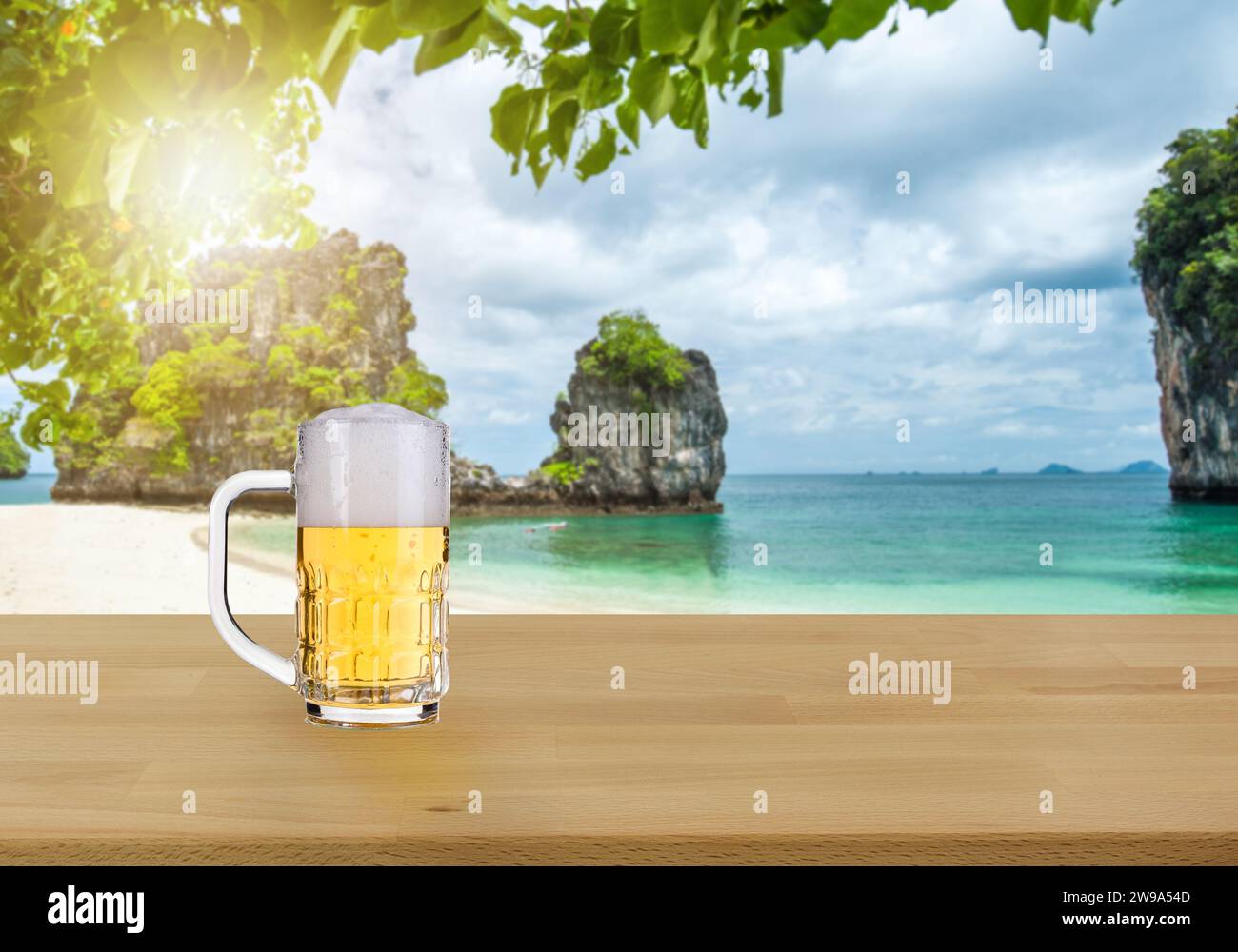 Beer is placed on a wooden table and view of tropical blurred beach ...