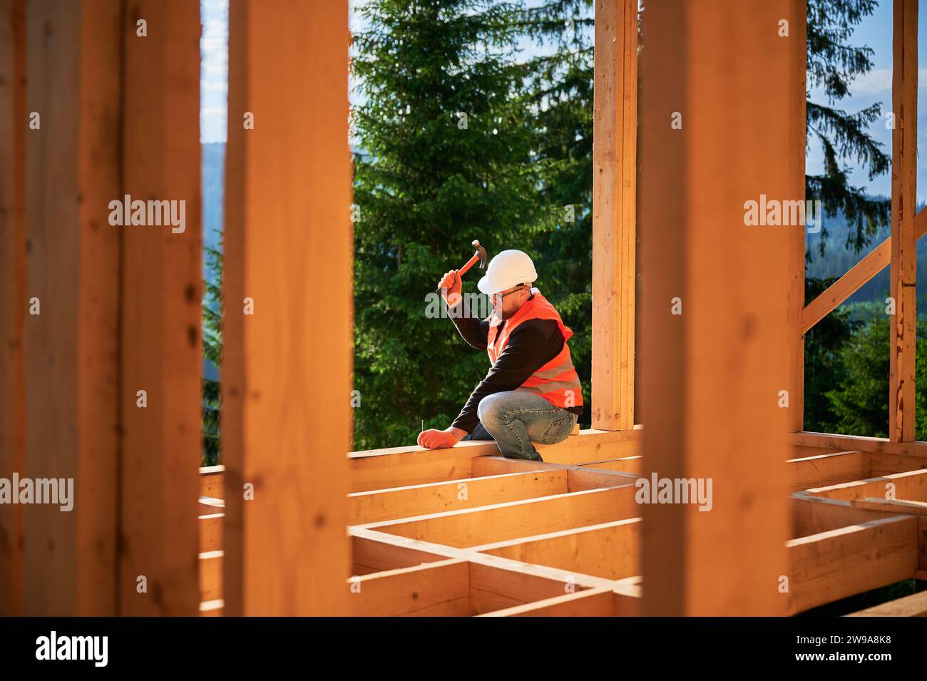Carpenter constructing two-story wooden frame house near forest. Man ...