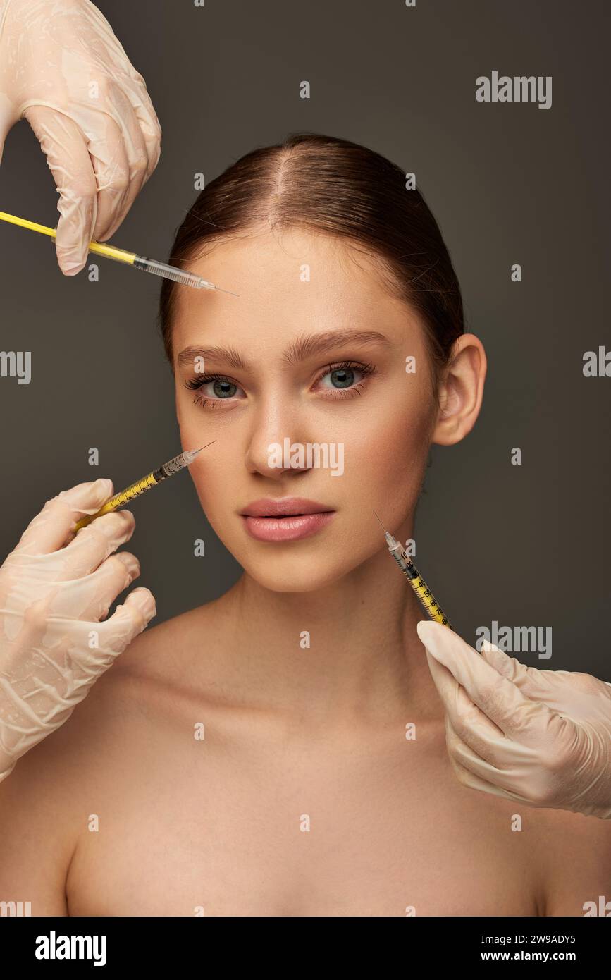 estheticians in medical gloves holding syringes near young woman on ...