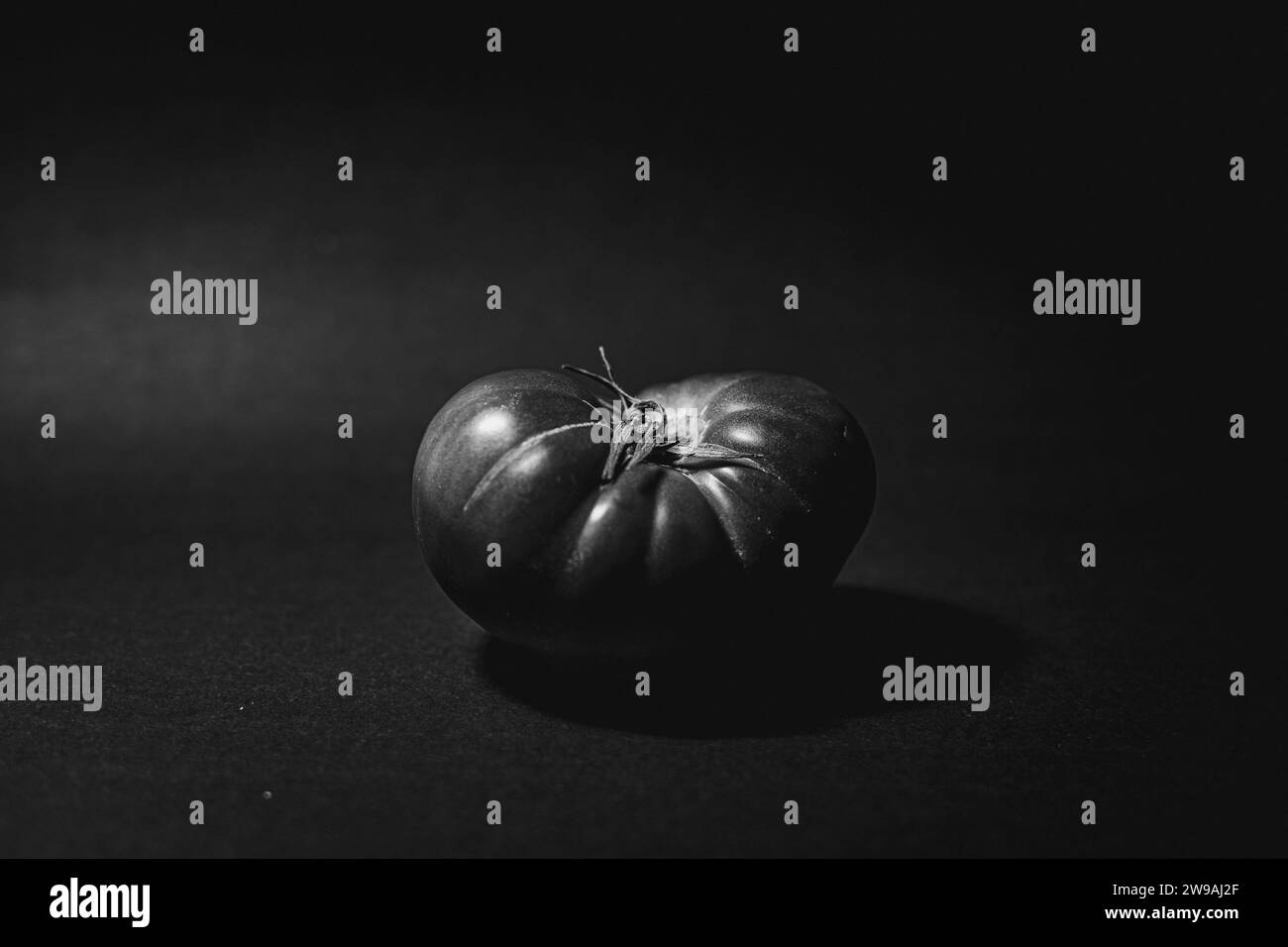 A grayscale shot of a ripe Spanish tomato on a solid tabletop, isolated ...