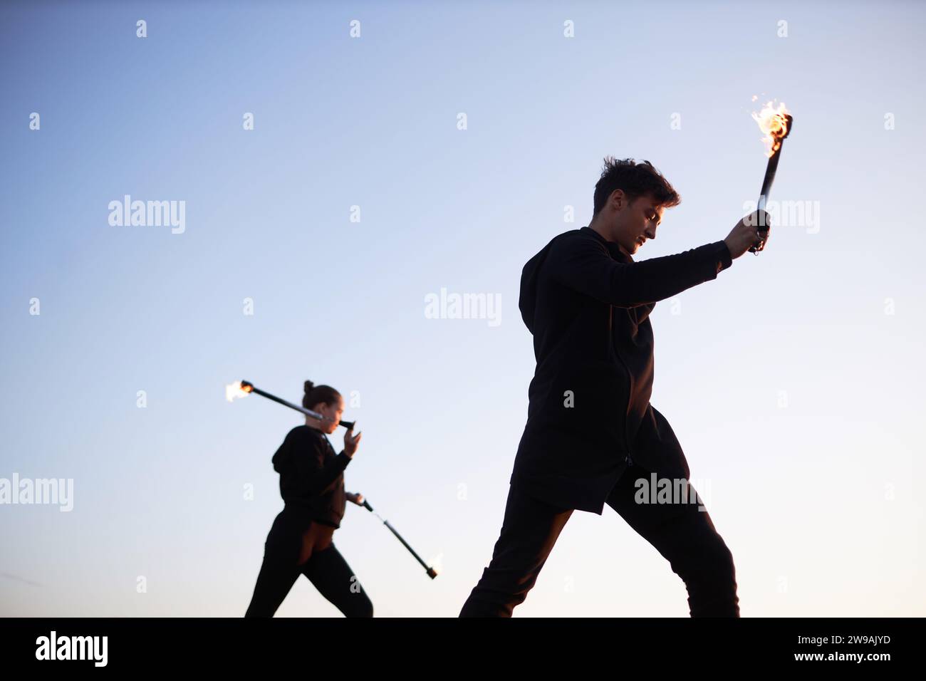 Side view at two fire show performers dancing with flames outdoors ...