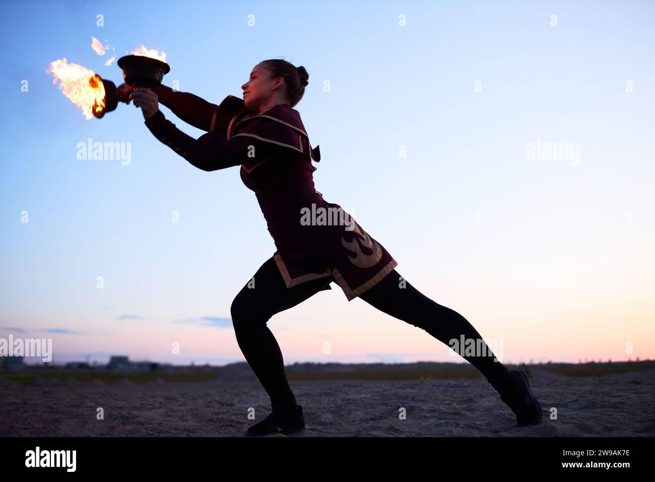 Side view portrait of female fire show performer dancing with flaming ...