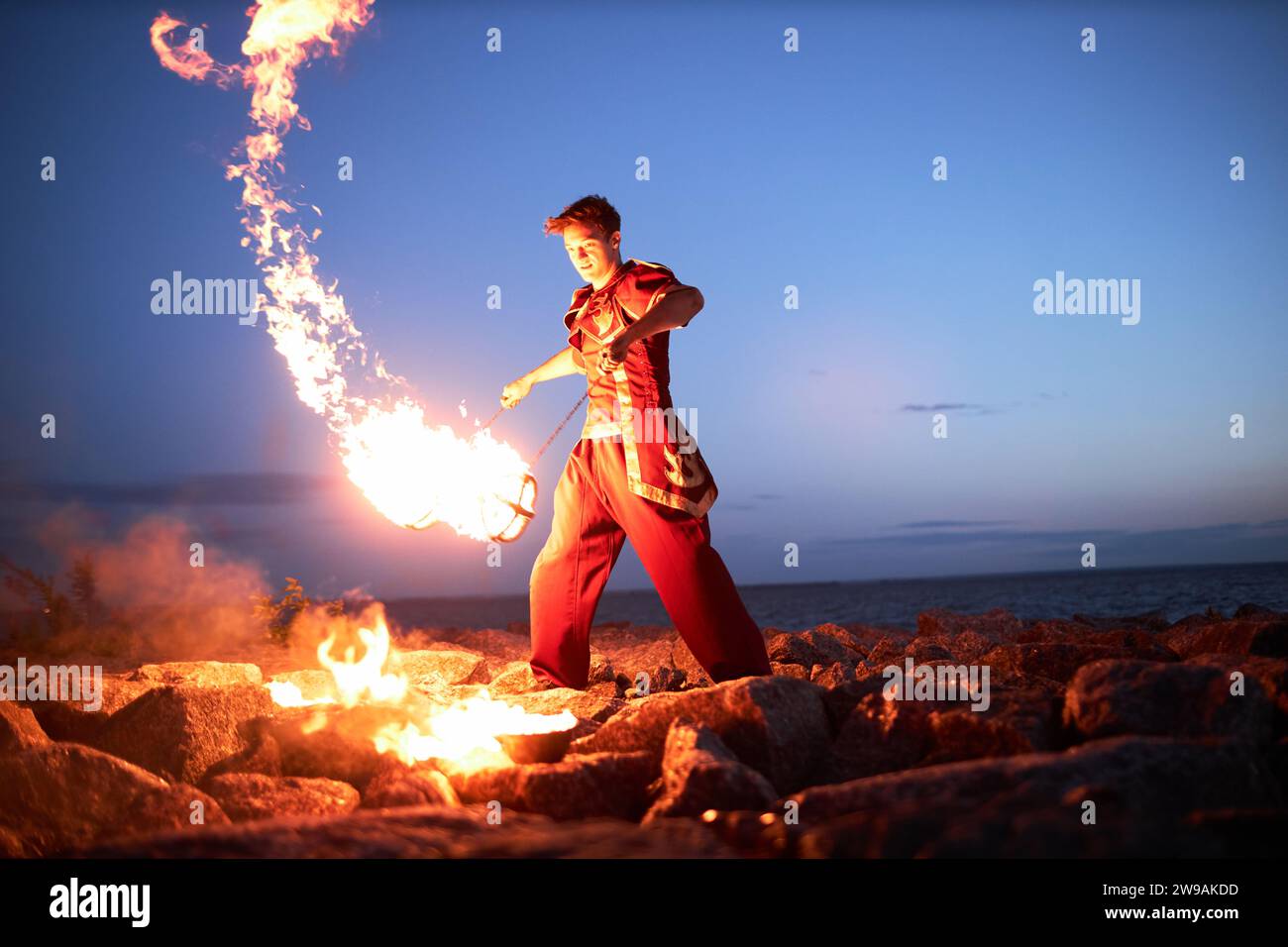 Full length portrait of young man juggling fire poi outdoors at night ...