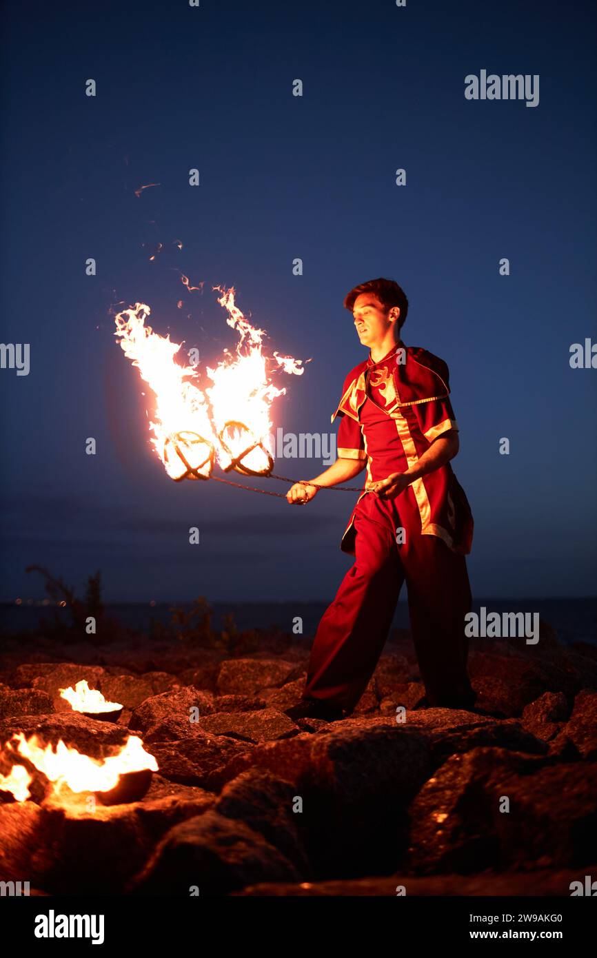 Full length portrait of fire show artist juggling fire poi outdoors at ...