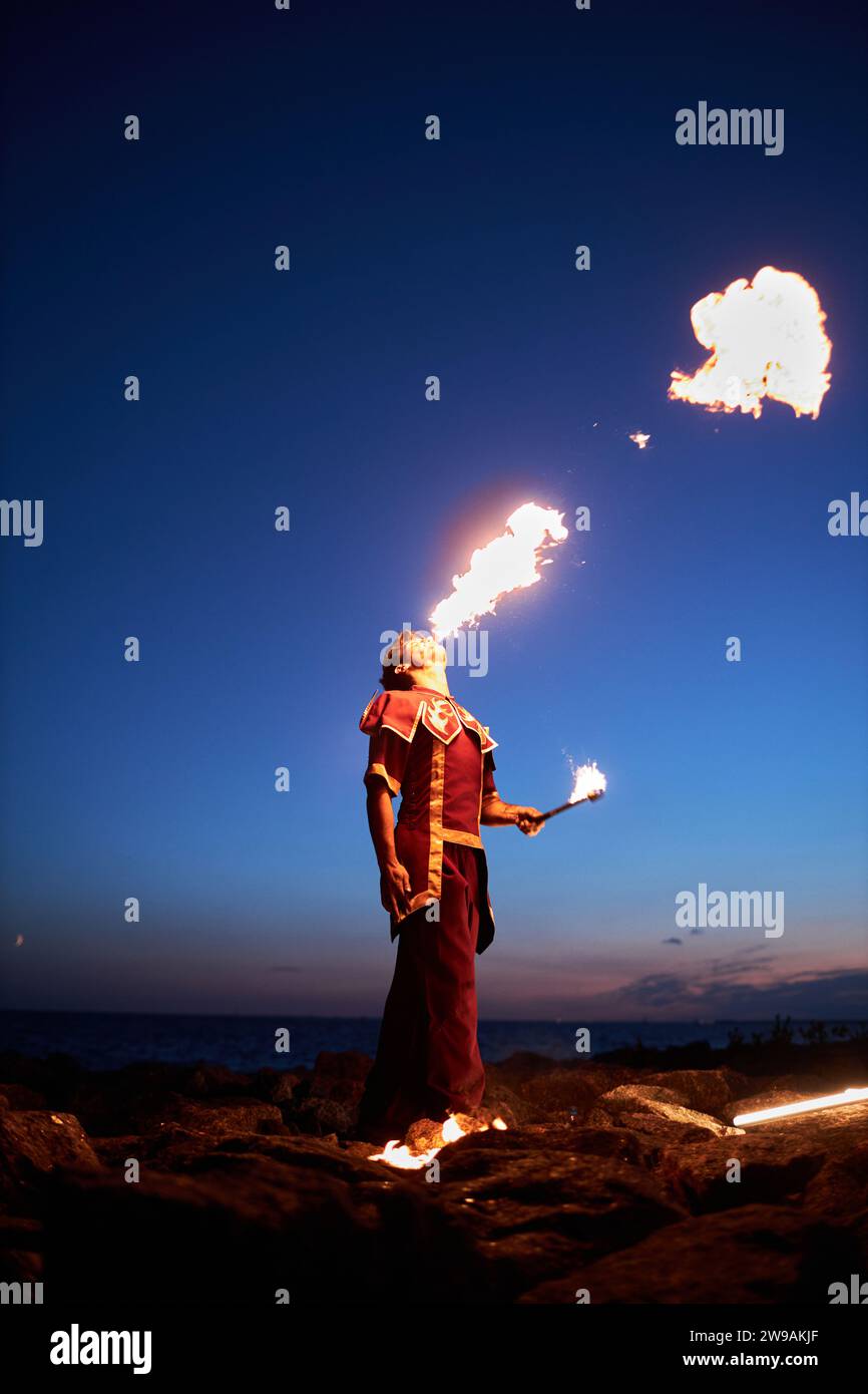 Vertical full length portrait of young man breathing fire against night ...