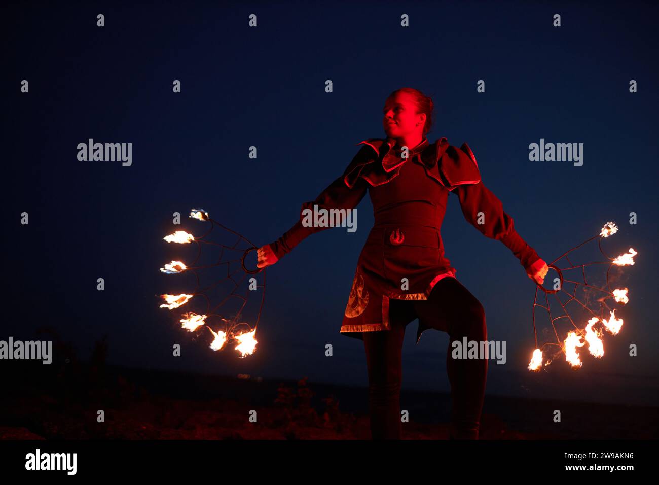 Full length portrait of performer dancing with fire fans outdoors at ...