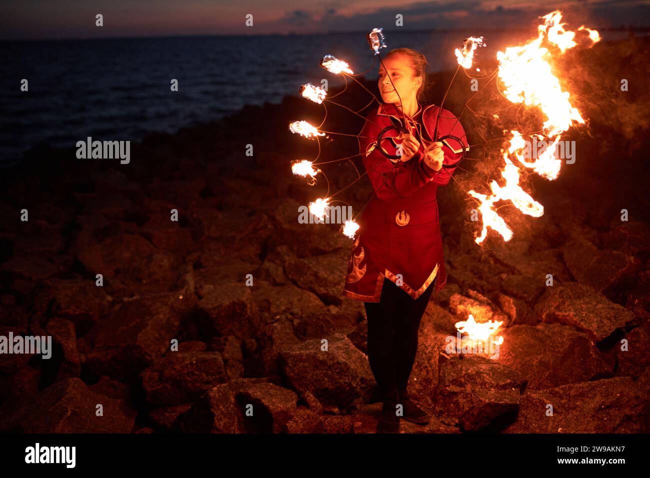 Full length portrait of young woman dancing with fire fans outdoors at ...