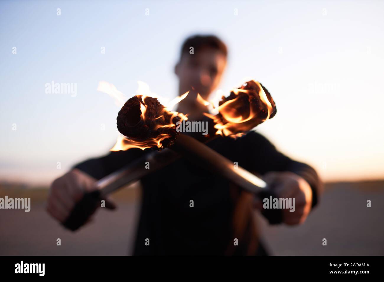 Close up of unrecognizable fire show performer crossing flaming rods to ...