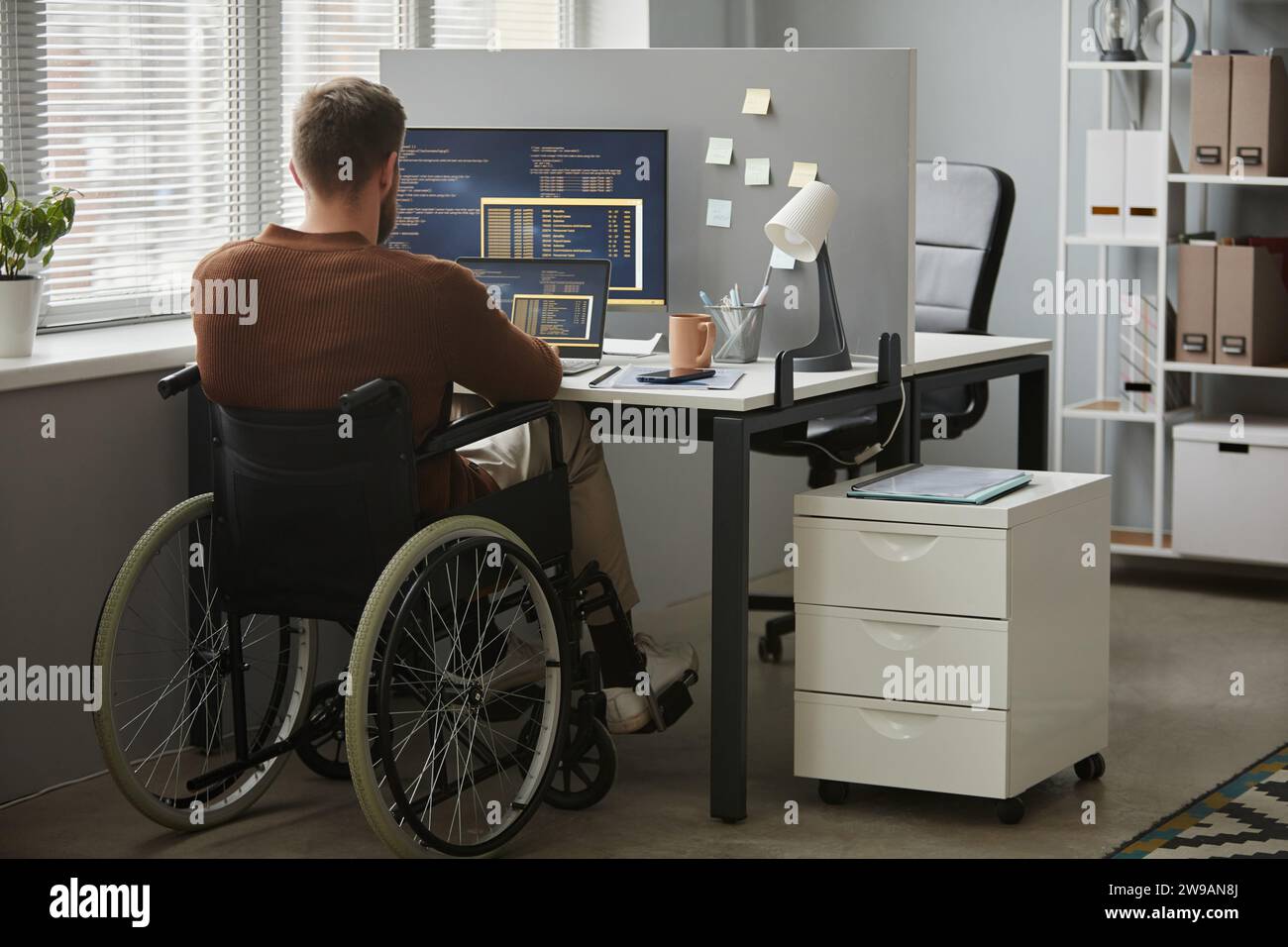 Back view of adult man with disability as computer programmer writing ...