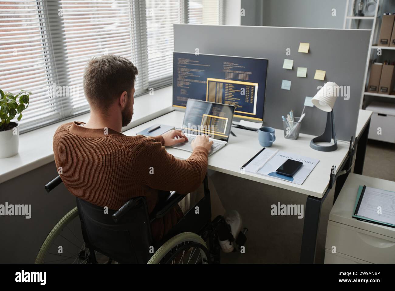Back view of adult man with disability using wheelchair at office ...