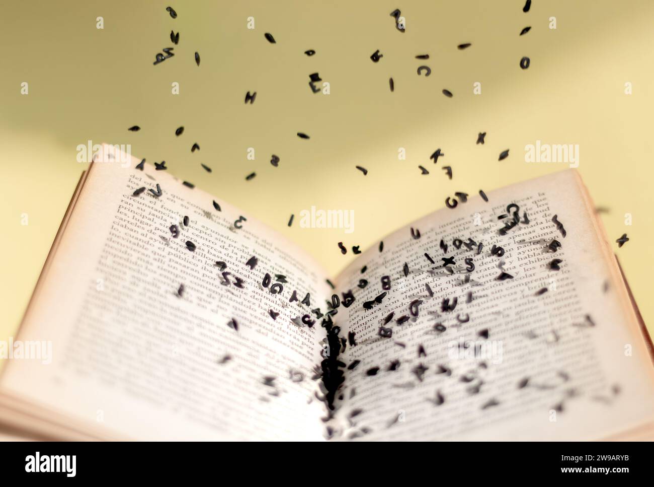 An open book on which black letters fall into it with a yellow ...