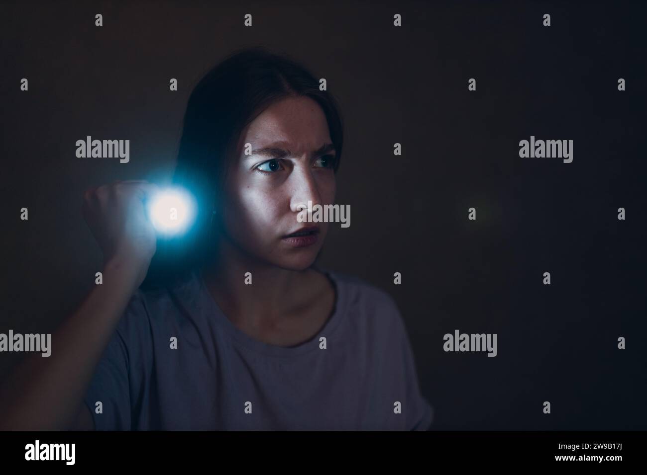 Woman scared holding hand flashlight in darkness and afraid of violence ...