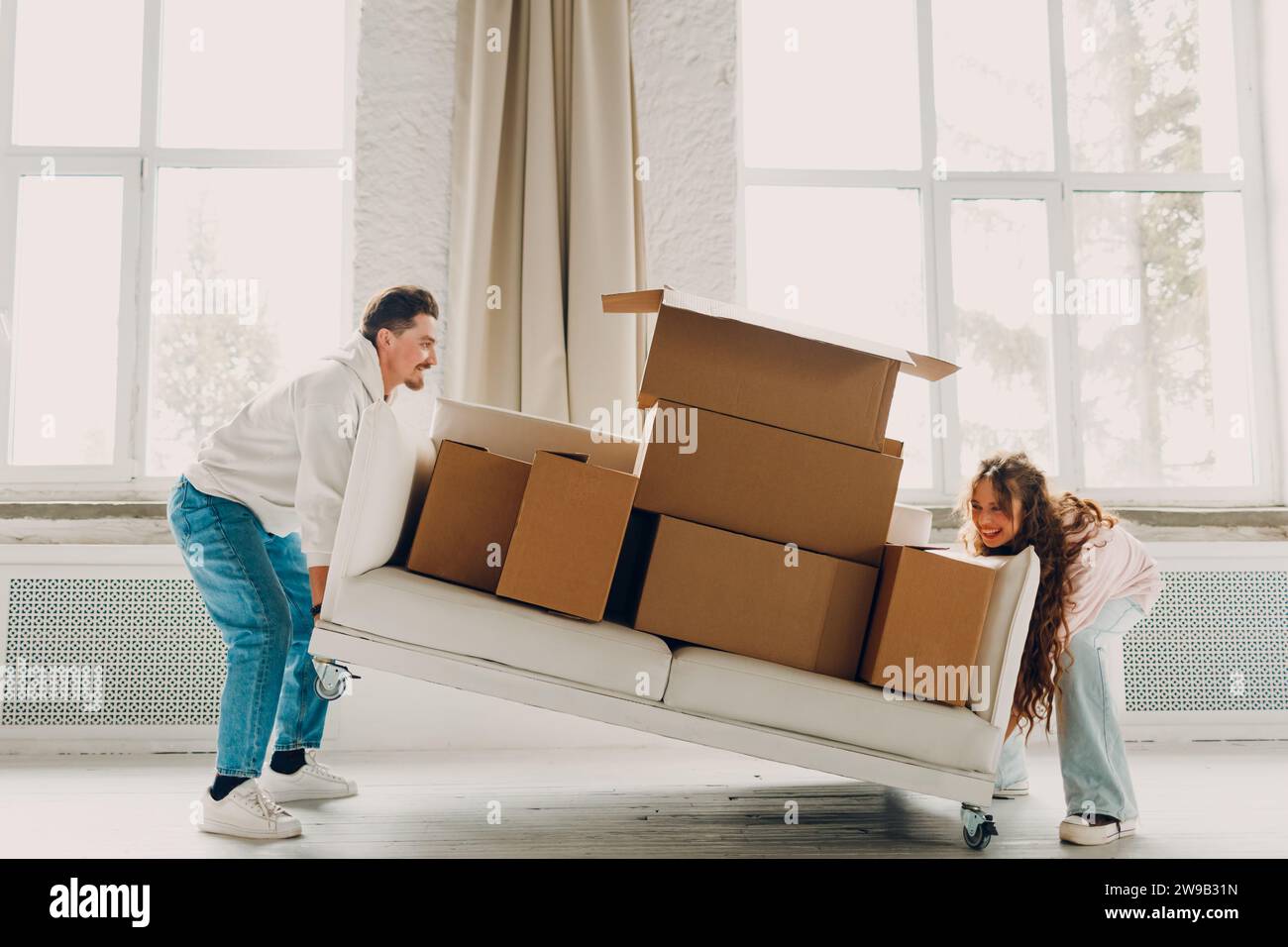 Happy young family couple man and woman lift and carry sofa with ...