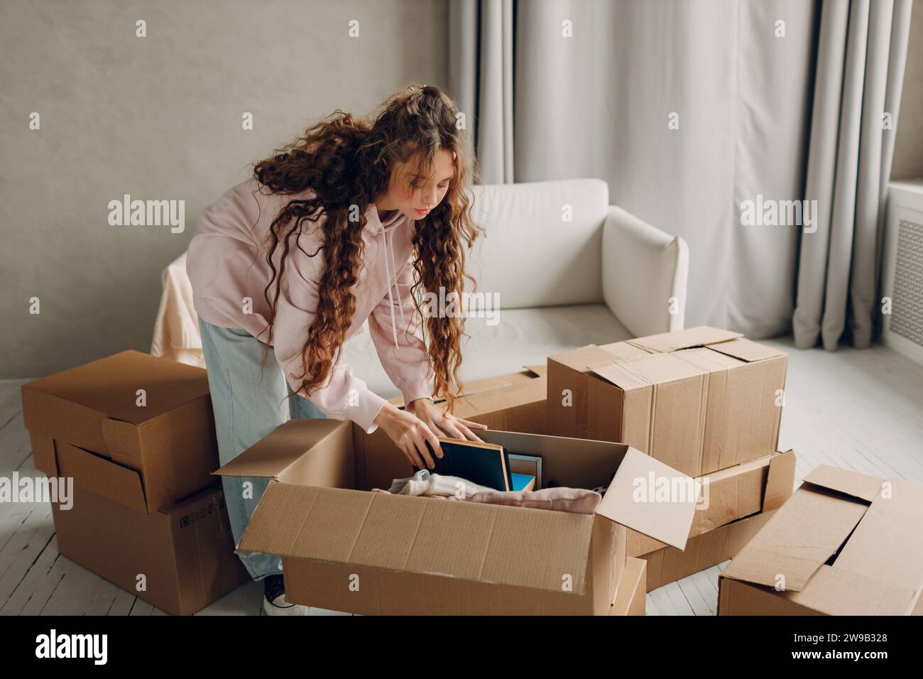 Happy young woman unpacking boxes with goods stuff after moving ...