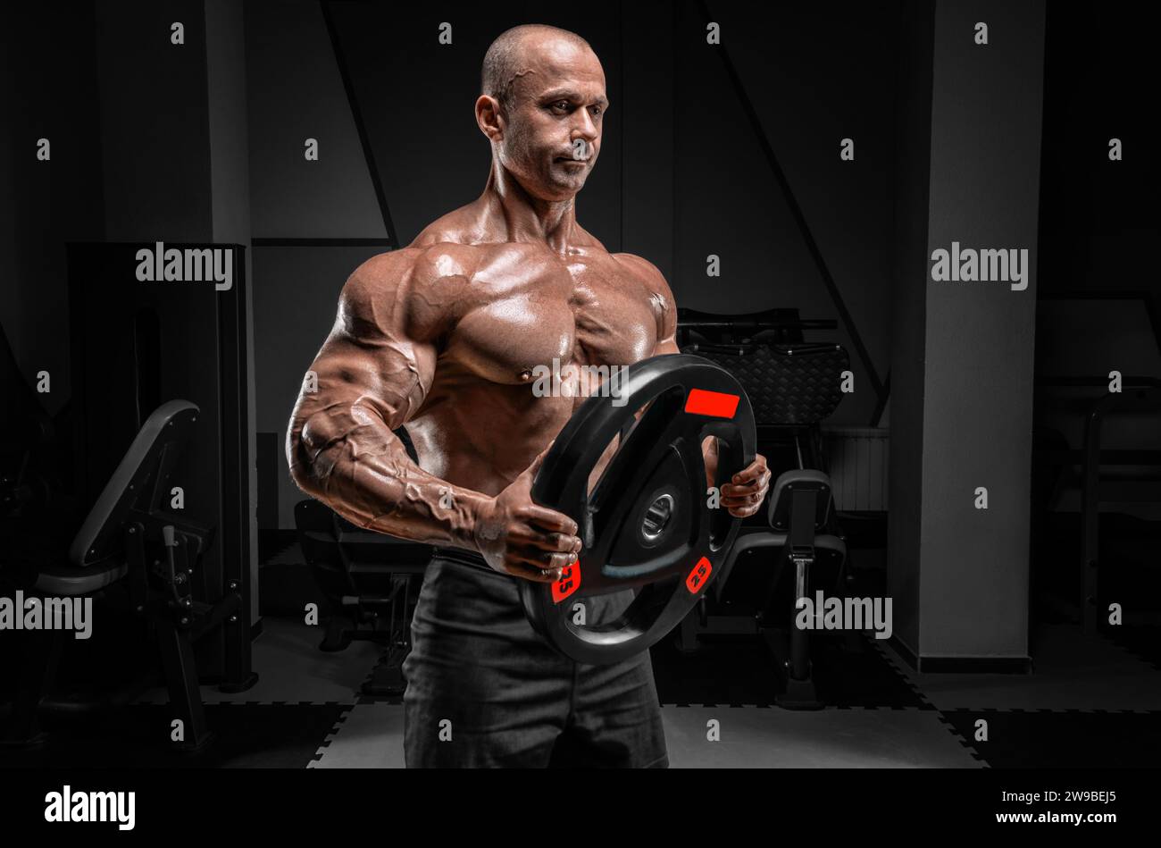 Muscular man posing in the gym with a barbell disc. Bodybuilding and ...