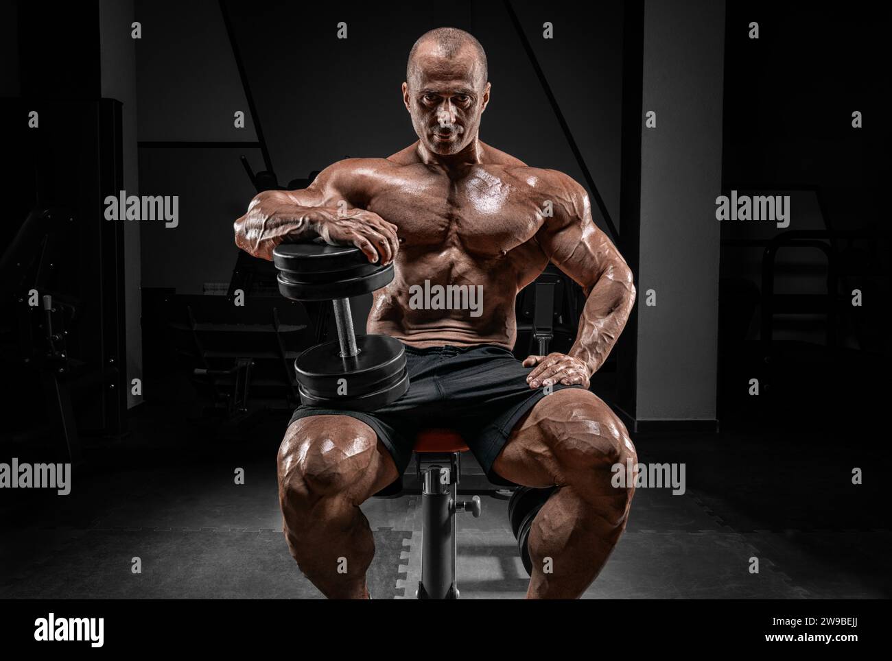 Muscular man sits on a bench with dumbbells. Bodybuilding and ...