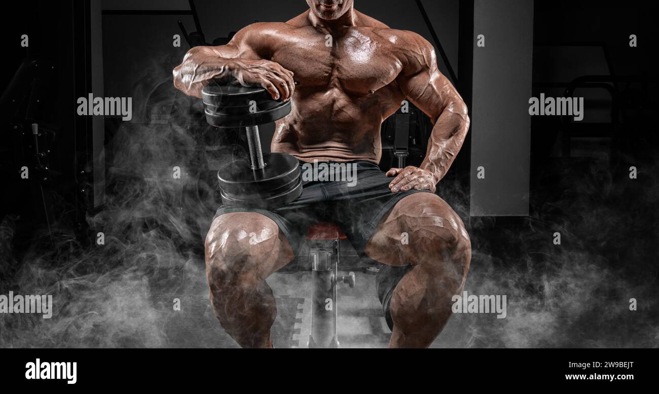 Muscular man sits on a bench in smoke with dumbbells. Bodybuilding and ...