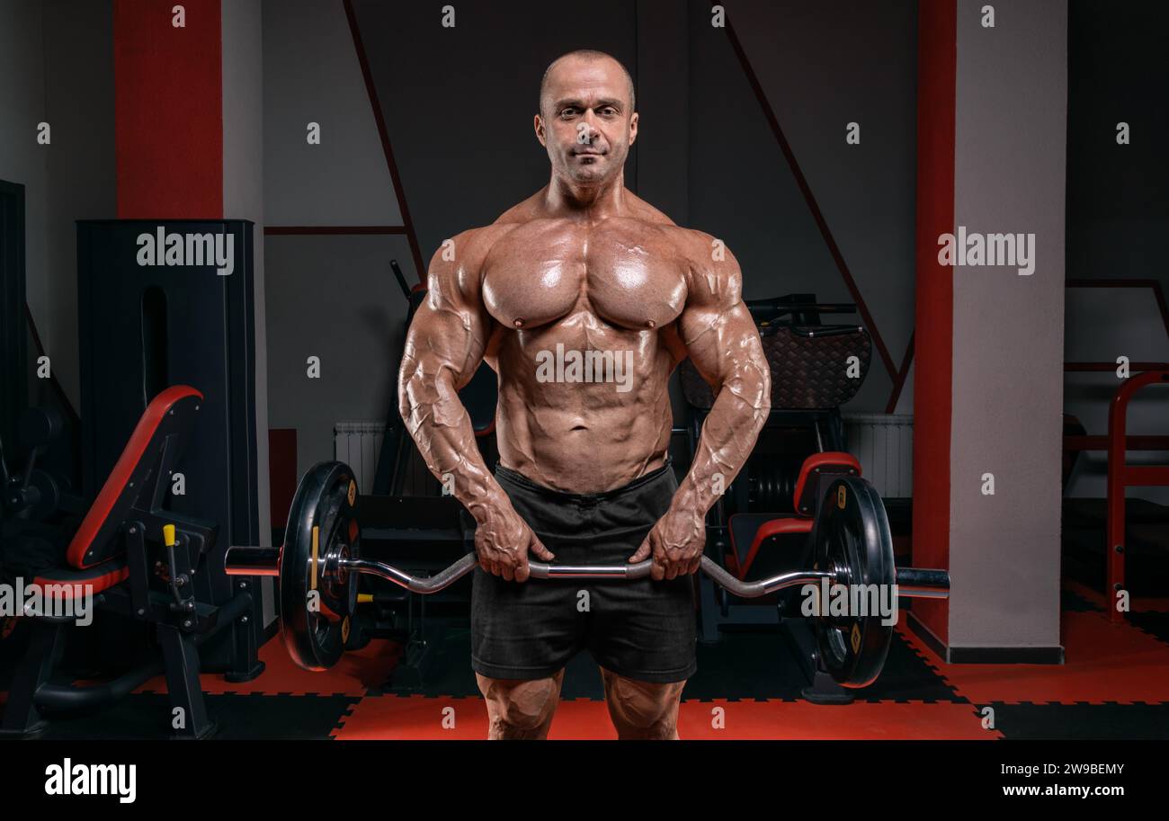 Powerful bodybuilder posing in the gym with a barbell. Bodybuilding ...