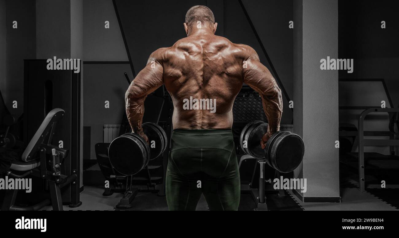Powerful bodybuilder posing in the gym with dumbbells. No name portrait ...