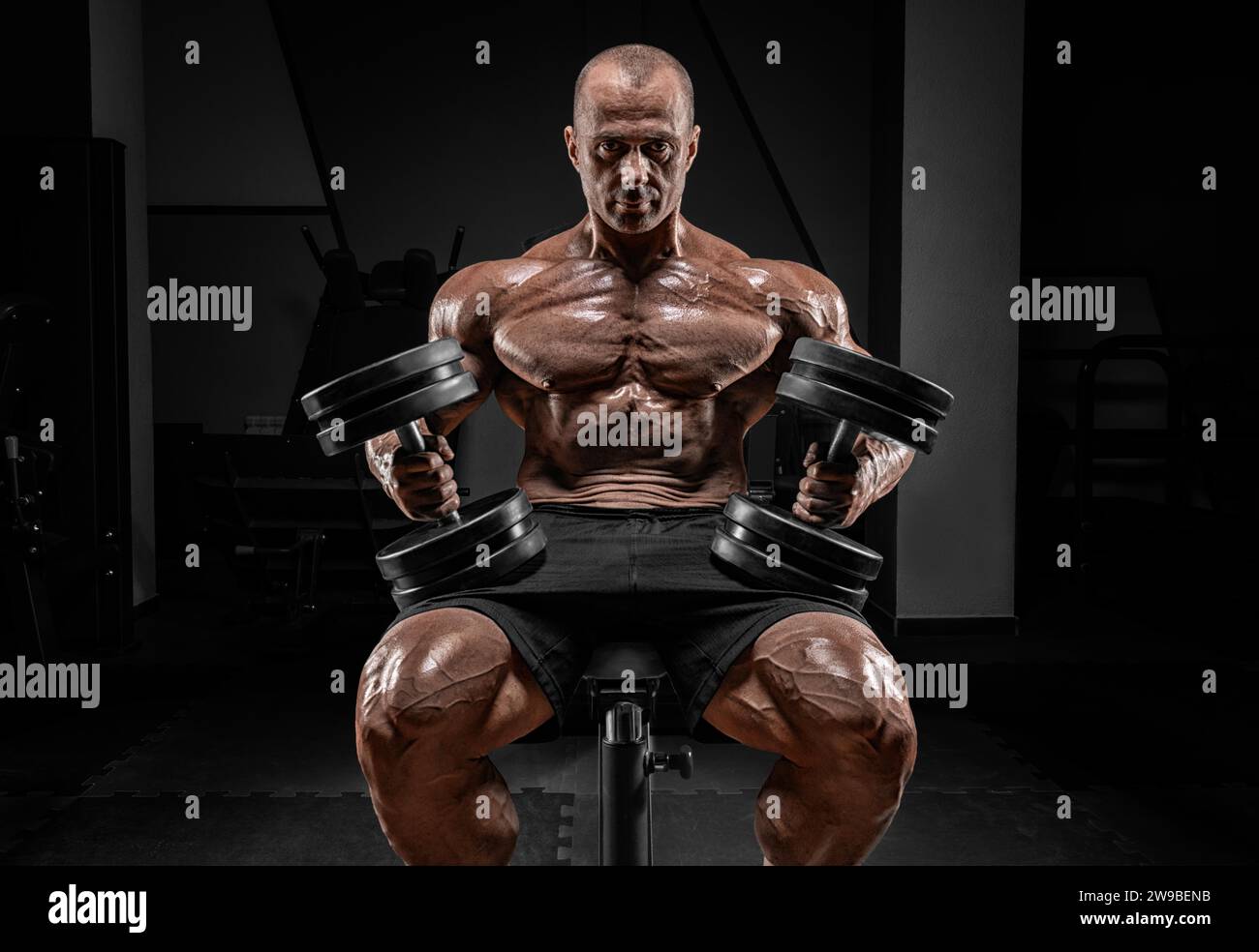 Muscular man sits on a bench with dumbbells. Bodybuilding and ...