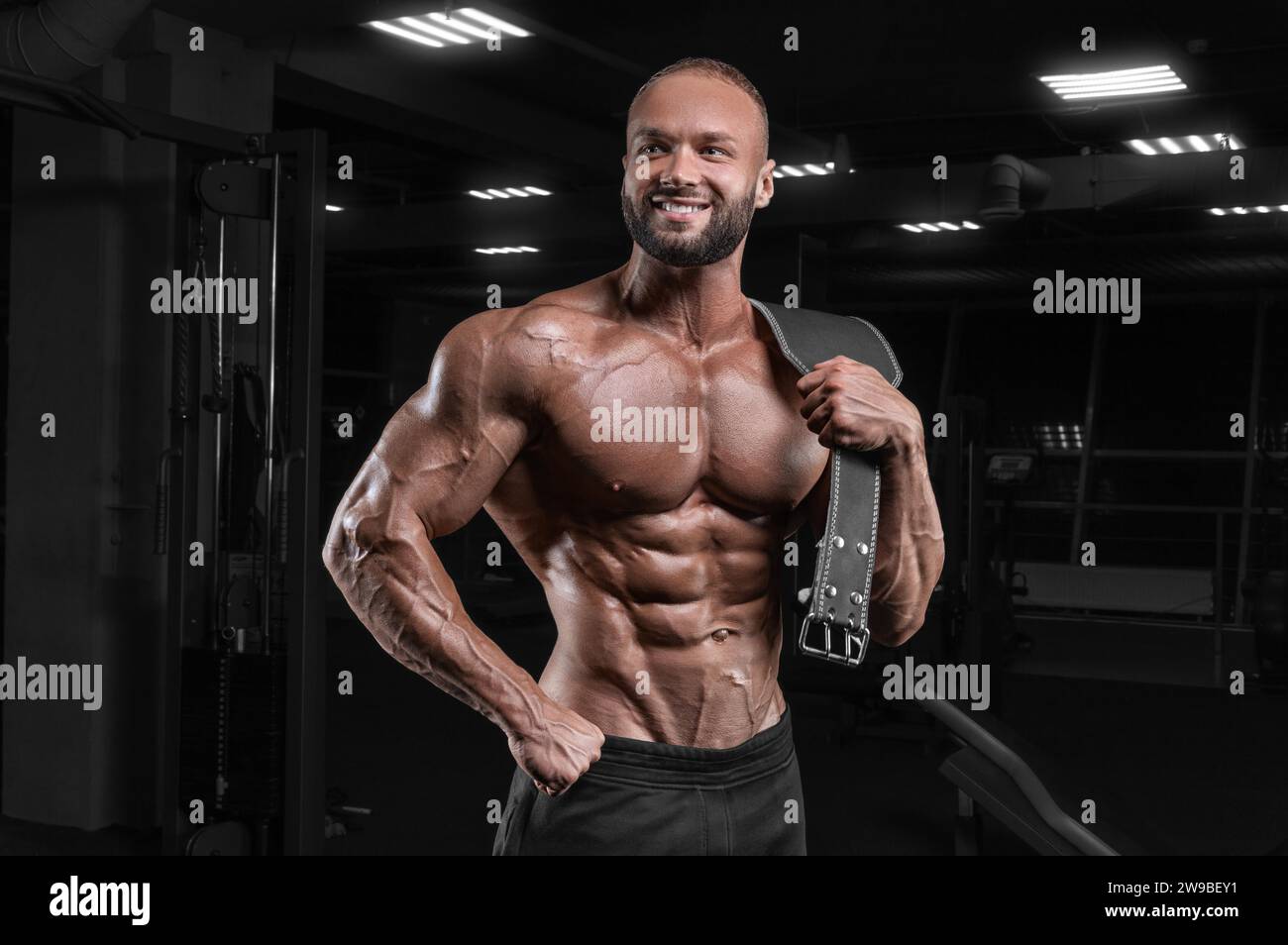 The athlete poses in the gym with an athletic belt. Fitness ...