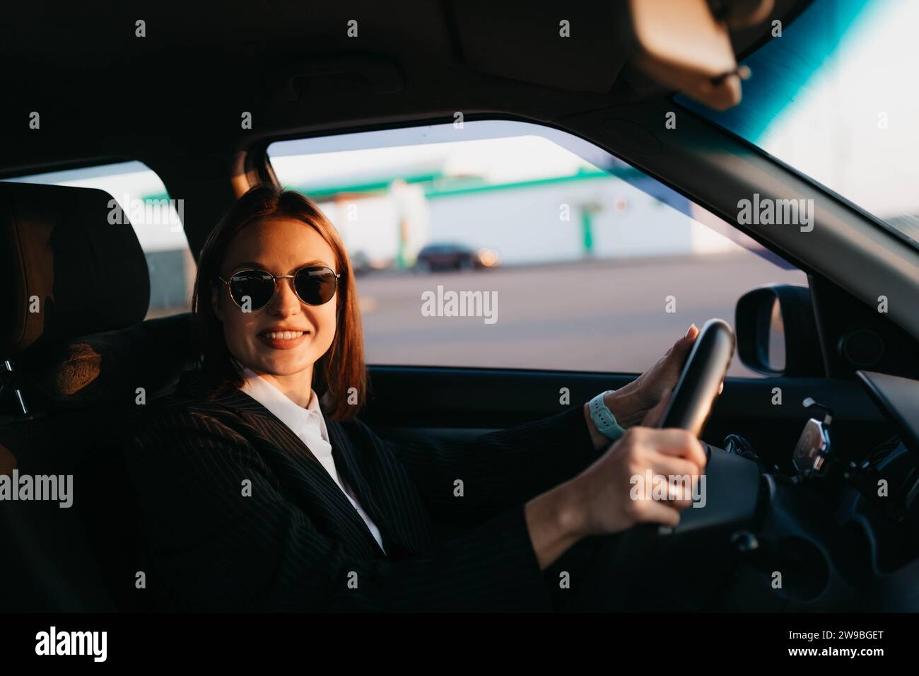 A young beautiful stylish girl driver in a jacket and sunglasses behind ...