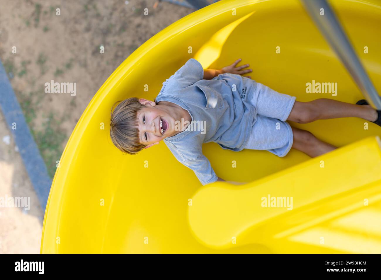 Top View. Portrait of laughing happy boy coming down slide, he looks up ...