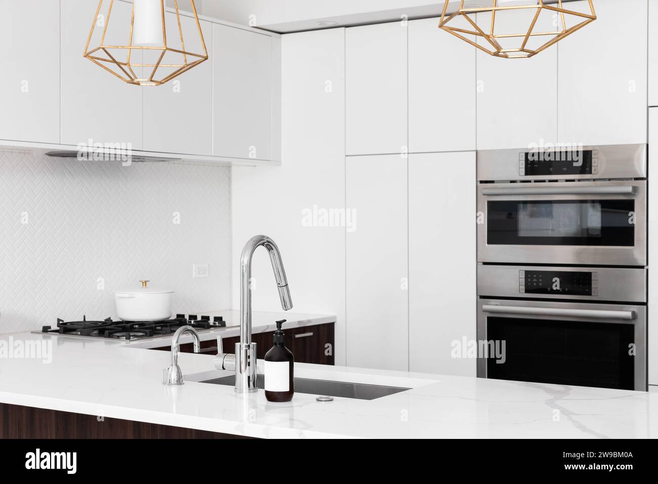 A chrome faucet detail in a white modern kitchen with gold light ...