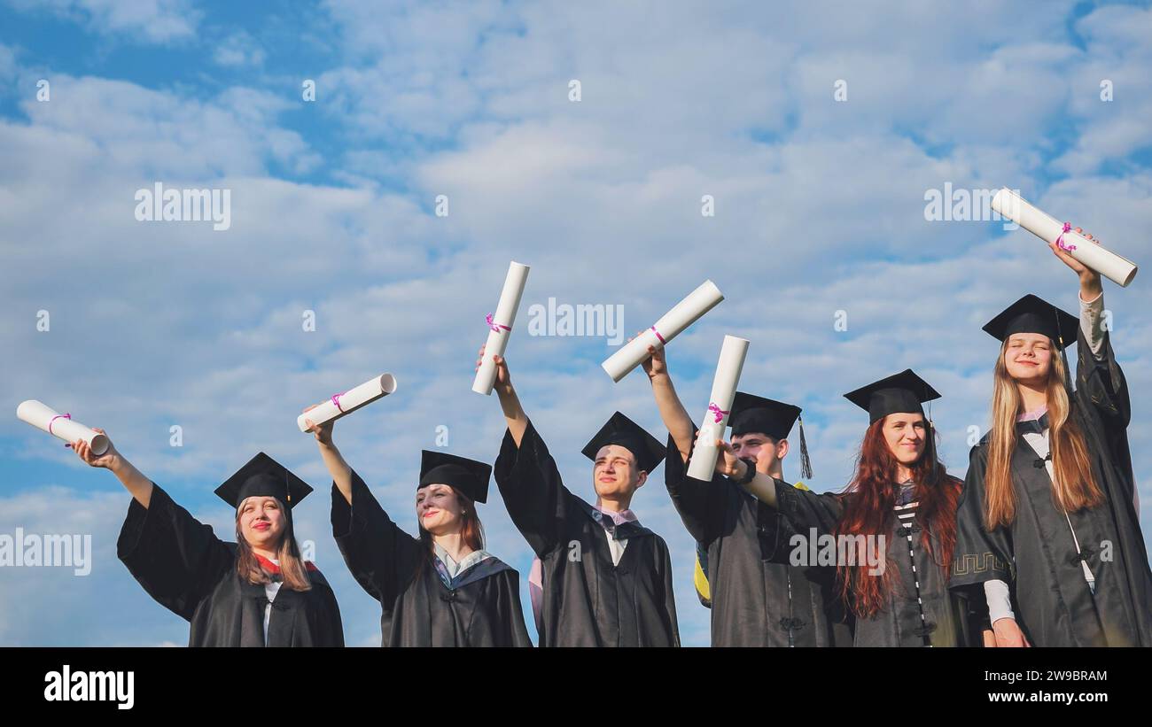 Cheerful graduates pose with raised diplomas on a sunny day Stock Photo ...