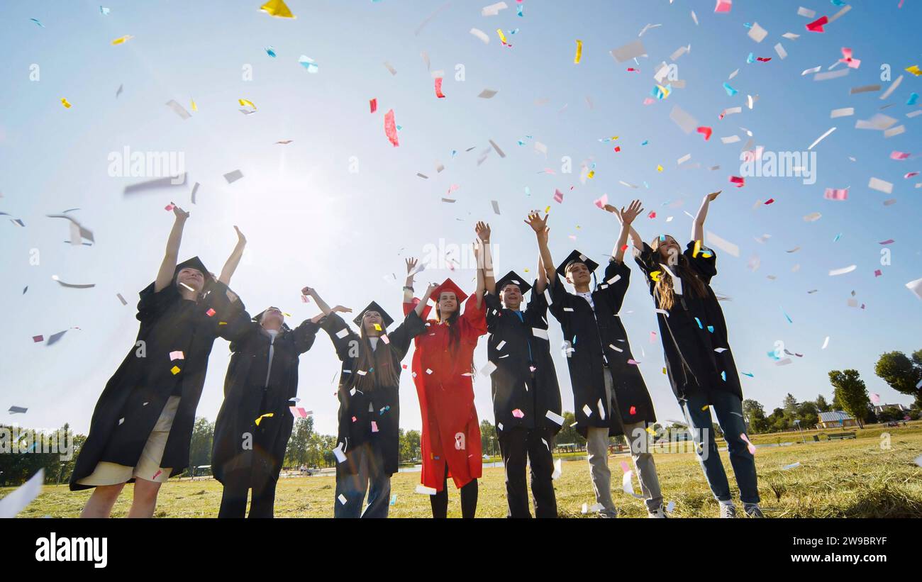 Happy college graduates throw colorful confetti against the rays of ...
