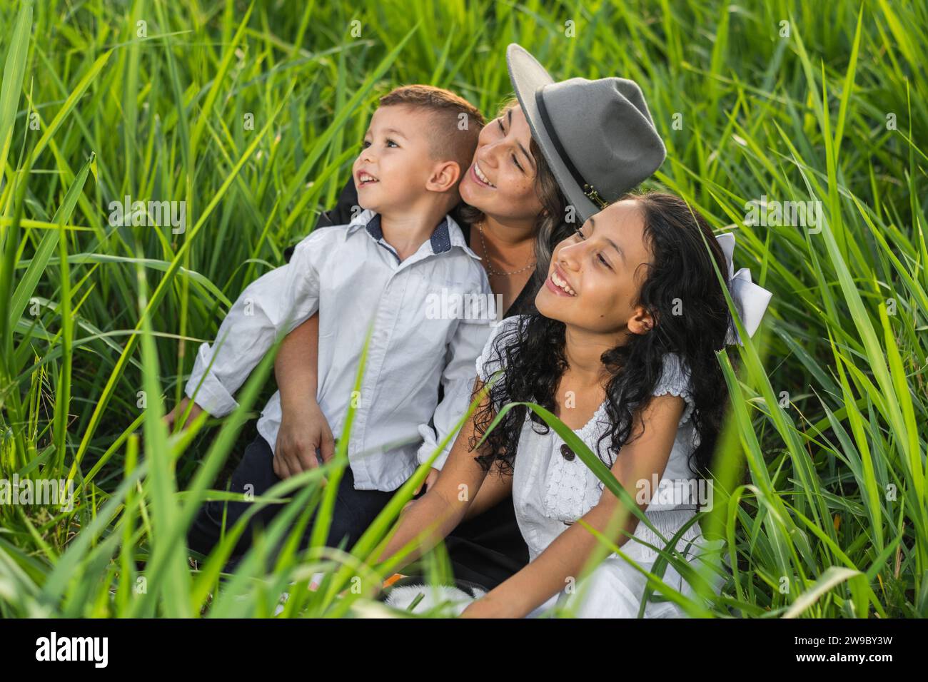 Latin family, young mother with her two children sitting on the grass ...