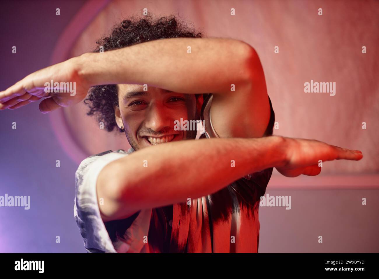 Young smiling man posing for camera with arms bent at elbows in front ...