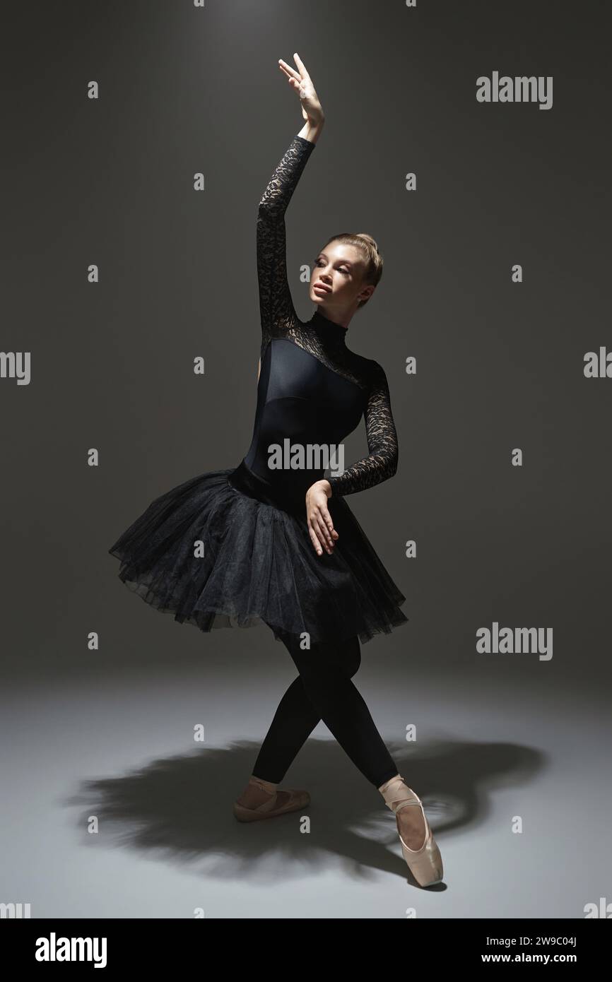 Young ballerina doing light lunge with her arm lift, posing against dim ...