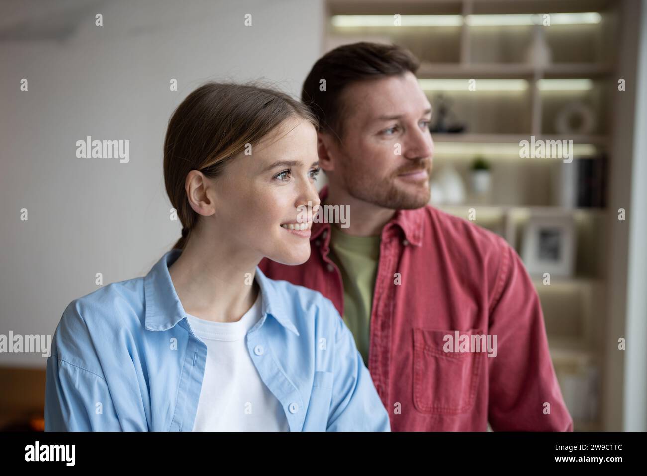 Happy family couple look at window together discussing something ...