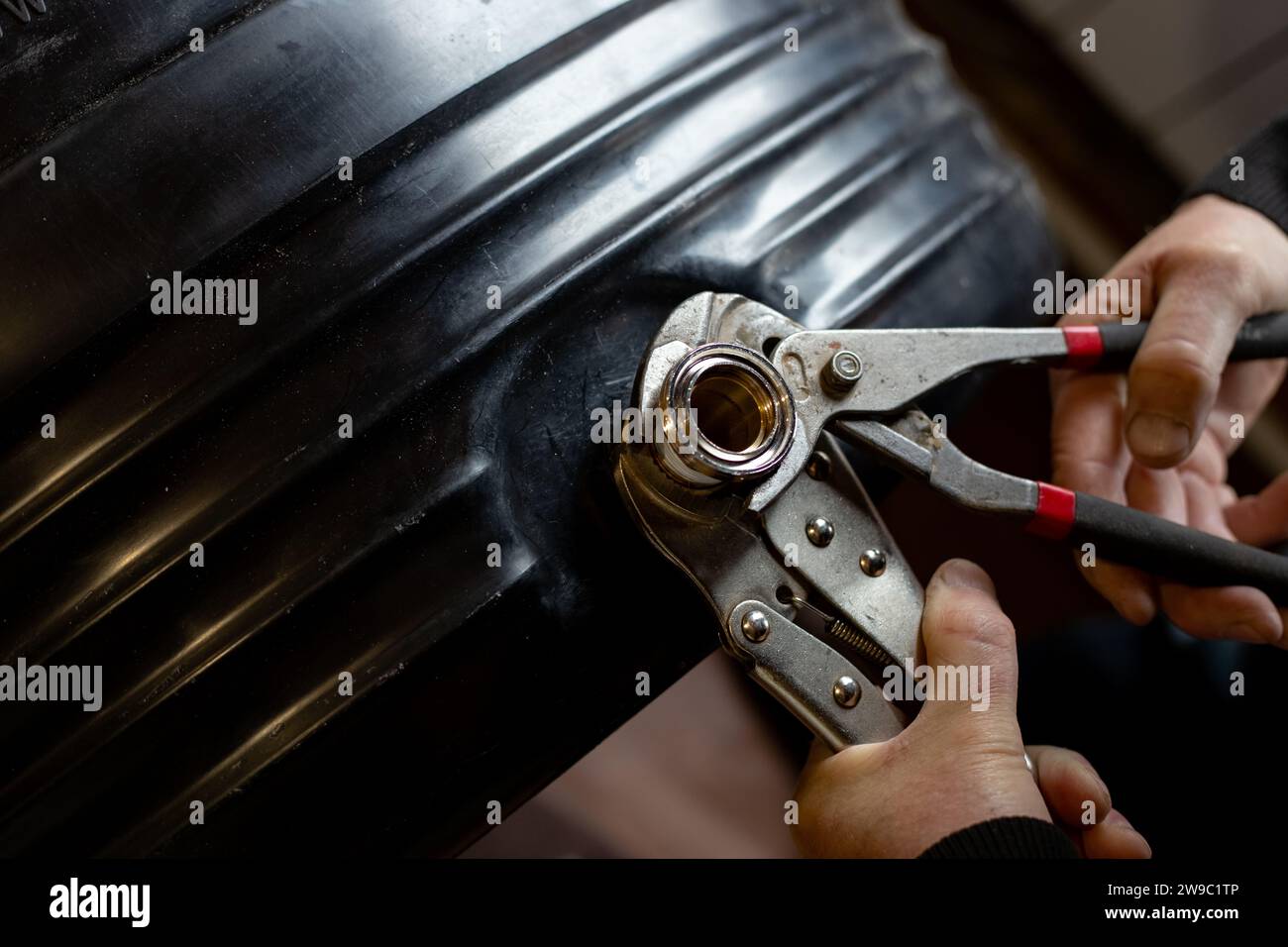 A plumber screws a fitting onto a water tank. Installation of a summer ...