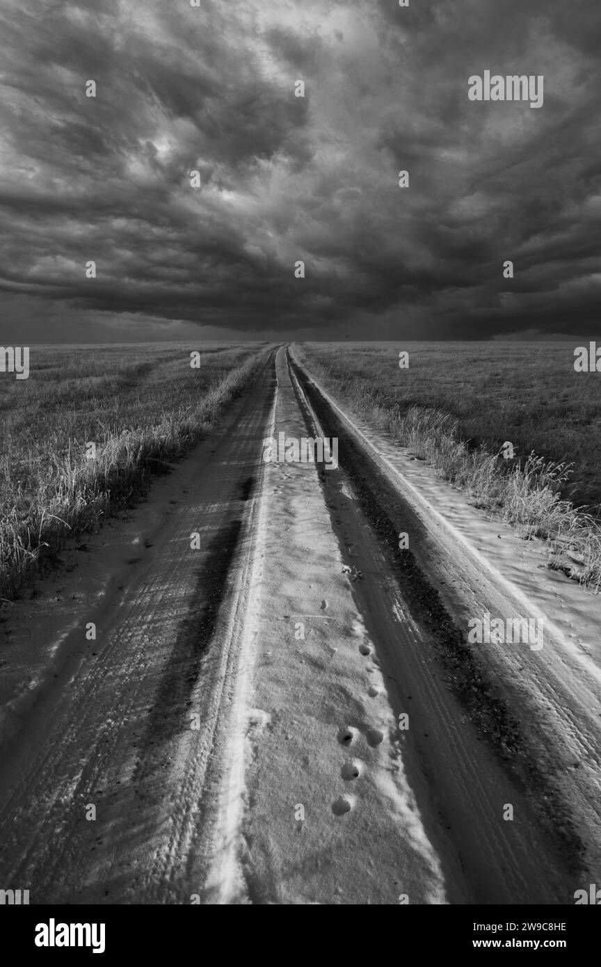 Snow covered dirt road through an empty field with storm clouds brewing ...