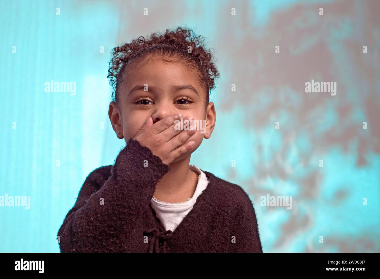 A young african-American girl holding her hand to her mouth as she ...