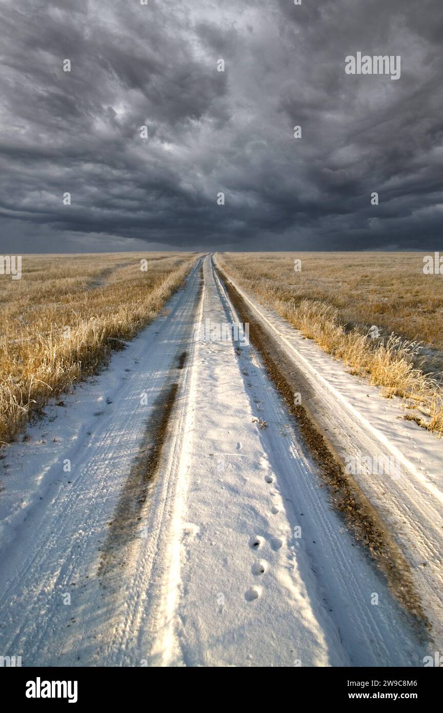 Snow covered dirt road through an empty field with storm clouds brewing ...