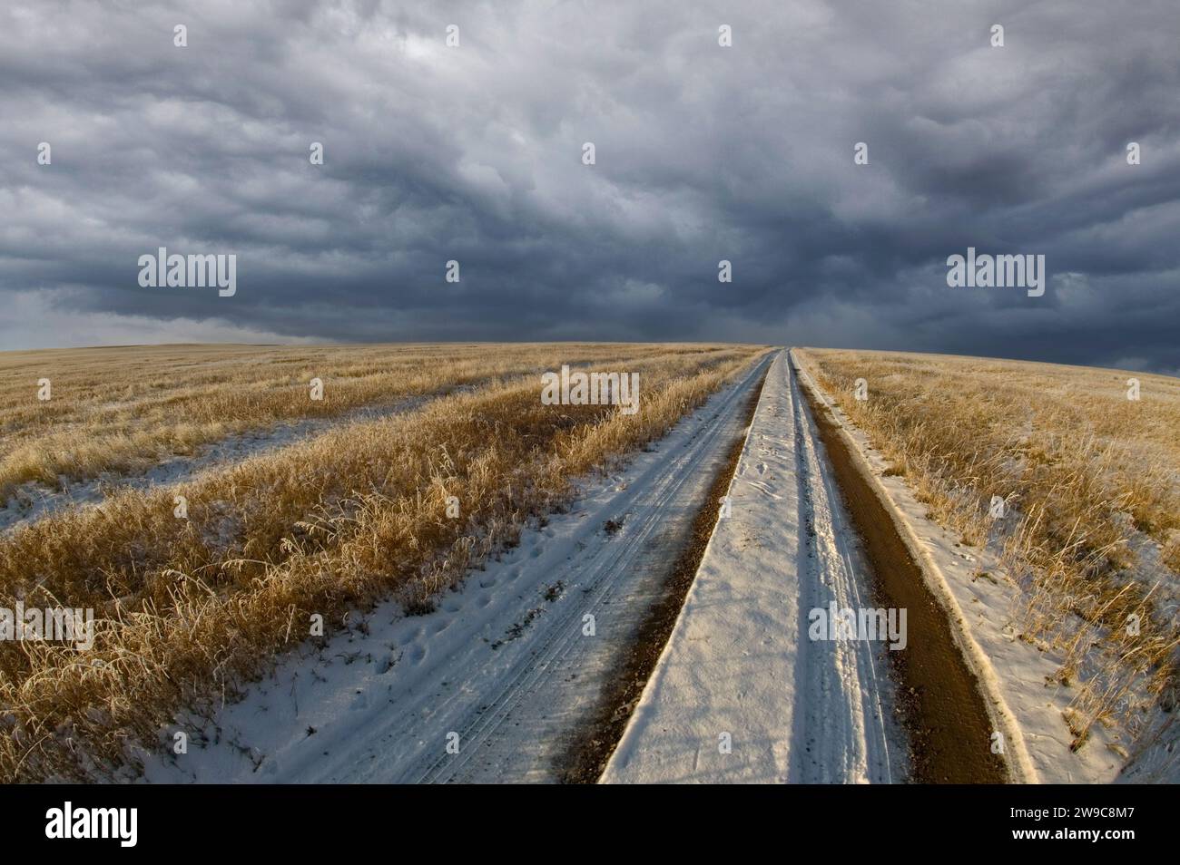 Snow covered dirt road through an empty field with storm clouds brewing ...