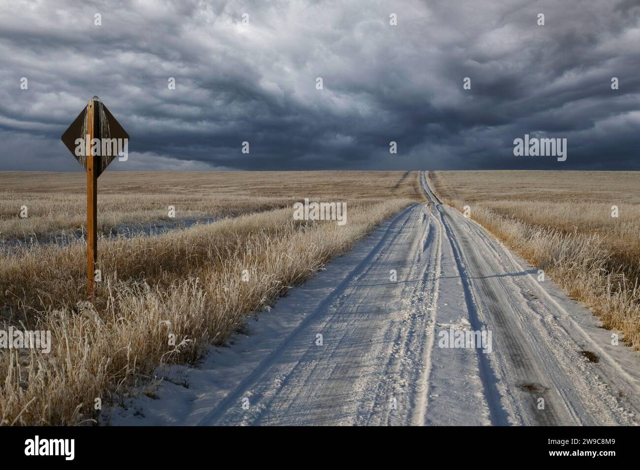 Snow covered dirt road through an empty field with storm clouds brewing ...