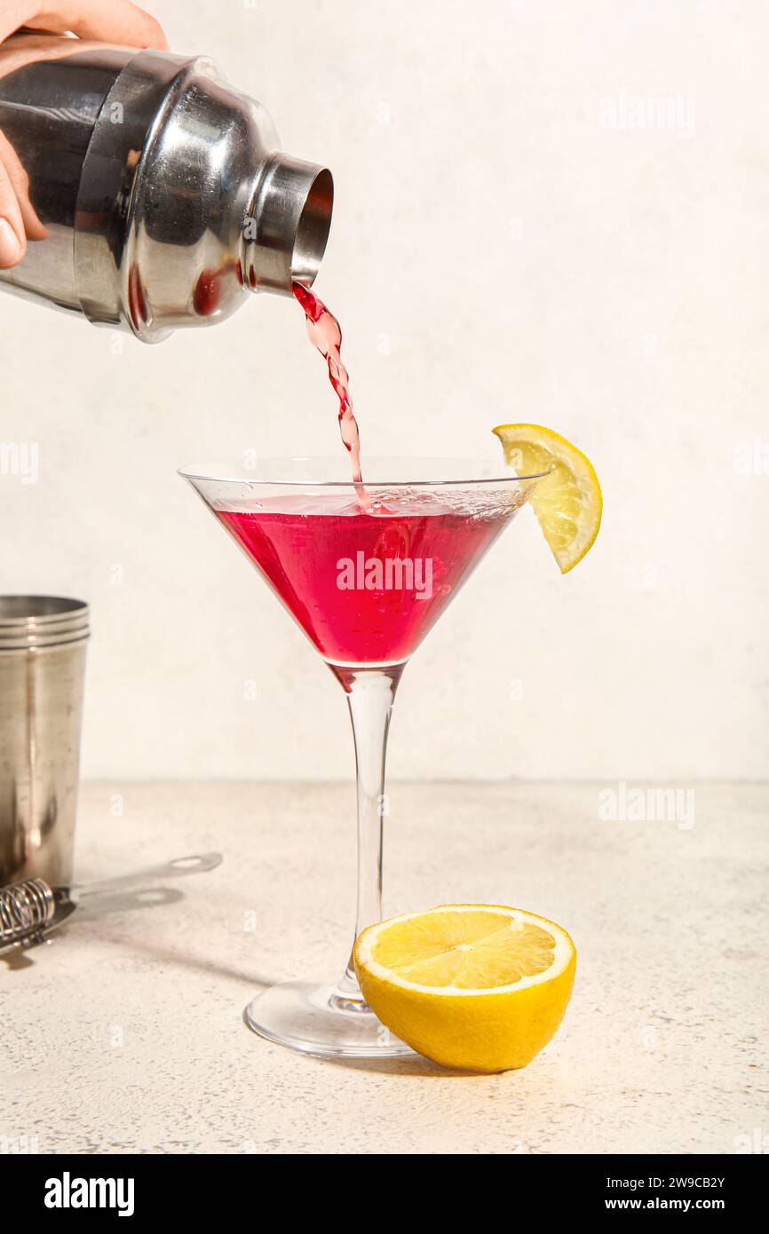 Woman pouring Cosmopolitan cocktail from shaker into glass on white ...
