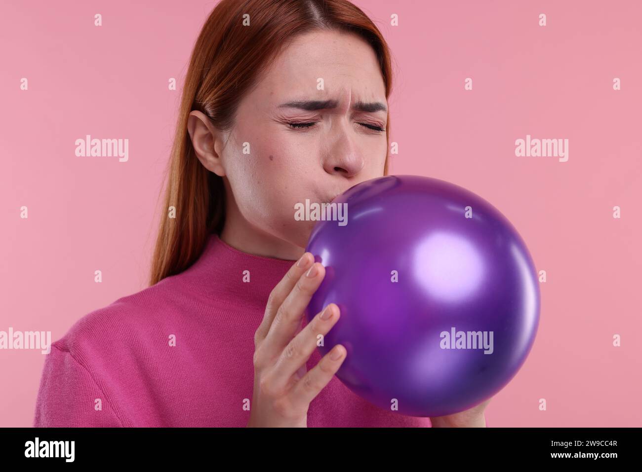 Woman inflating purple balloon on pink background Stock Photo - Alamy