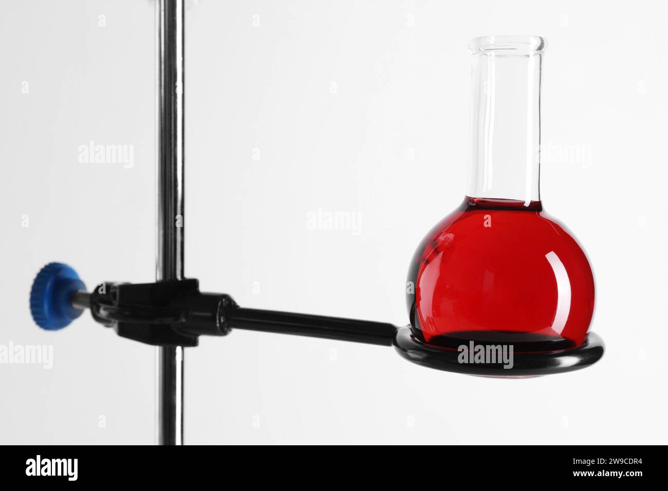 Retort stand and laboratory flask with liquid on white background ...