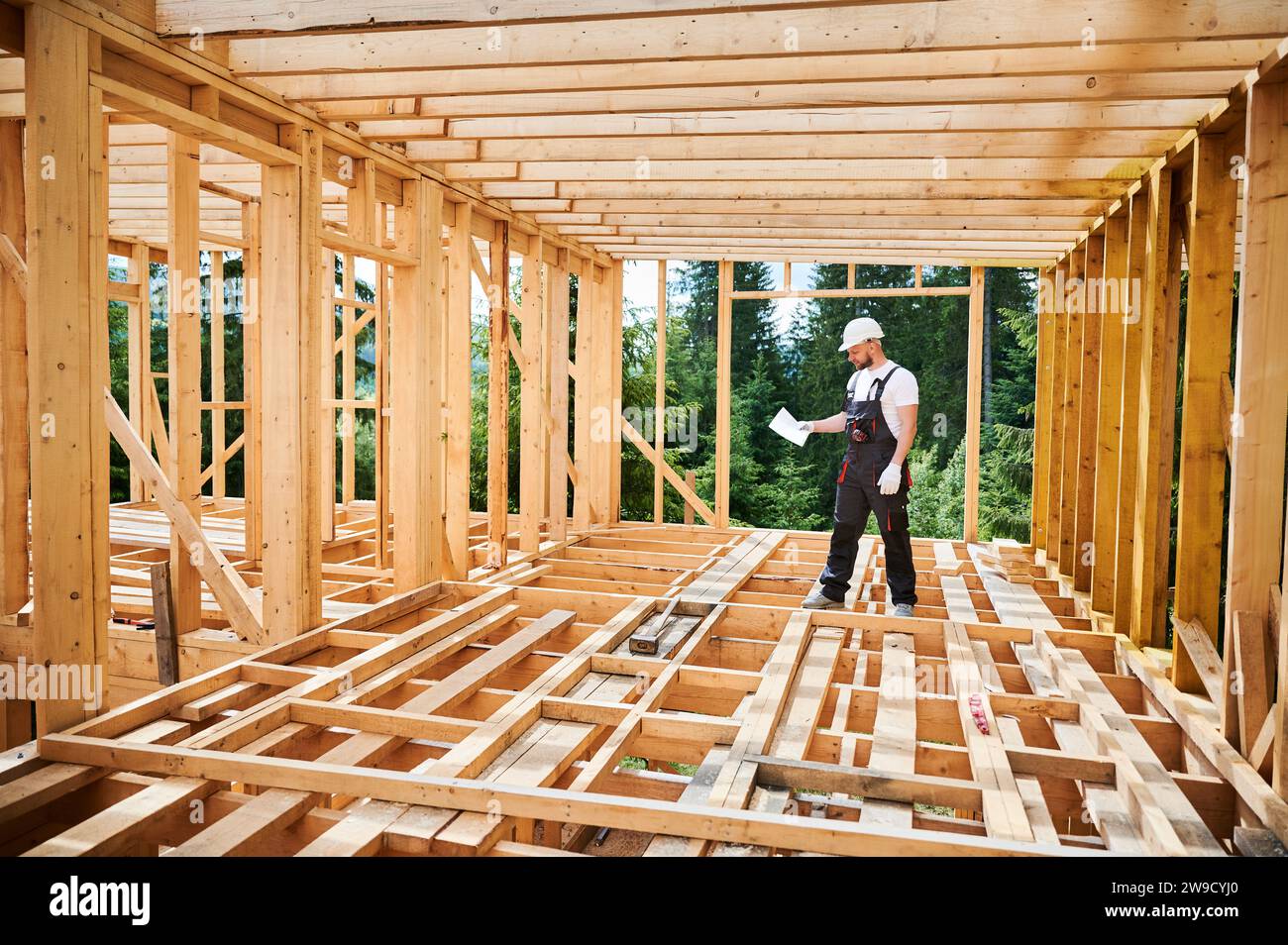 Worker building wooden two-story house near the forest. Man in work ...