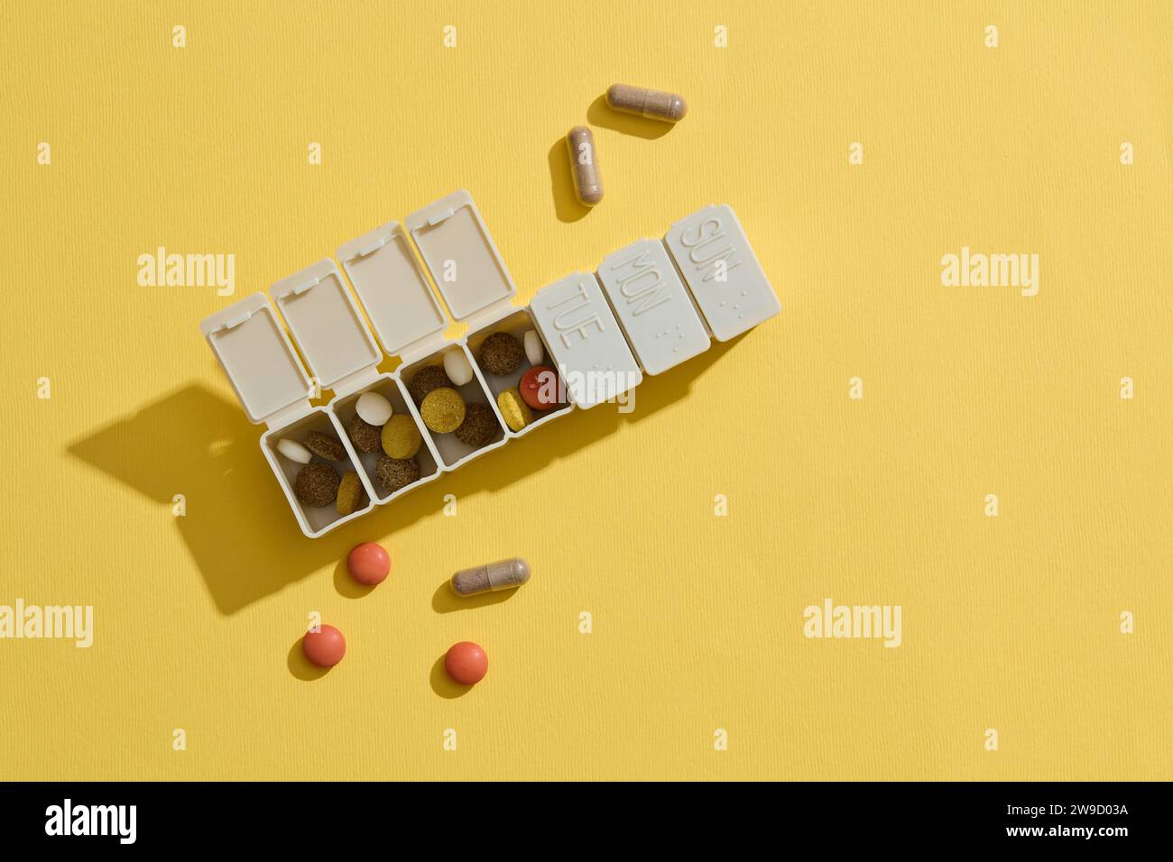 Against the yellow background, the plastic box containing pills of ...