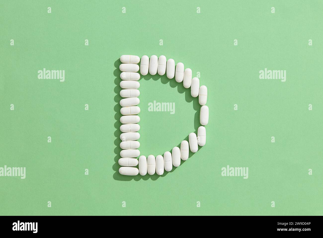 Vitamin D pills arranged in the shape of the letter D on a green ...